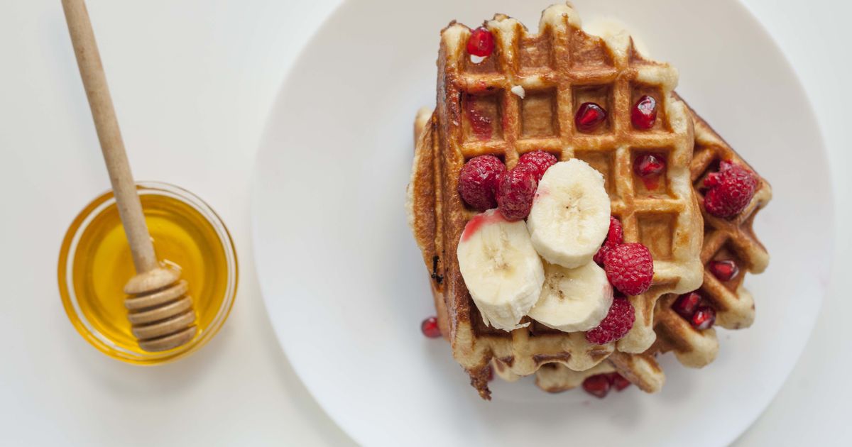 Vafe belgiene cu miere, rodie, zmeură și felii de banane deasupra ...